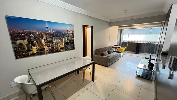 Uma sala de estar moderna com área de jantar, um sofá, uma mesa de vidro e uma grande pintura com vista para a cidade.