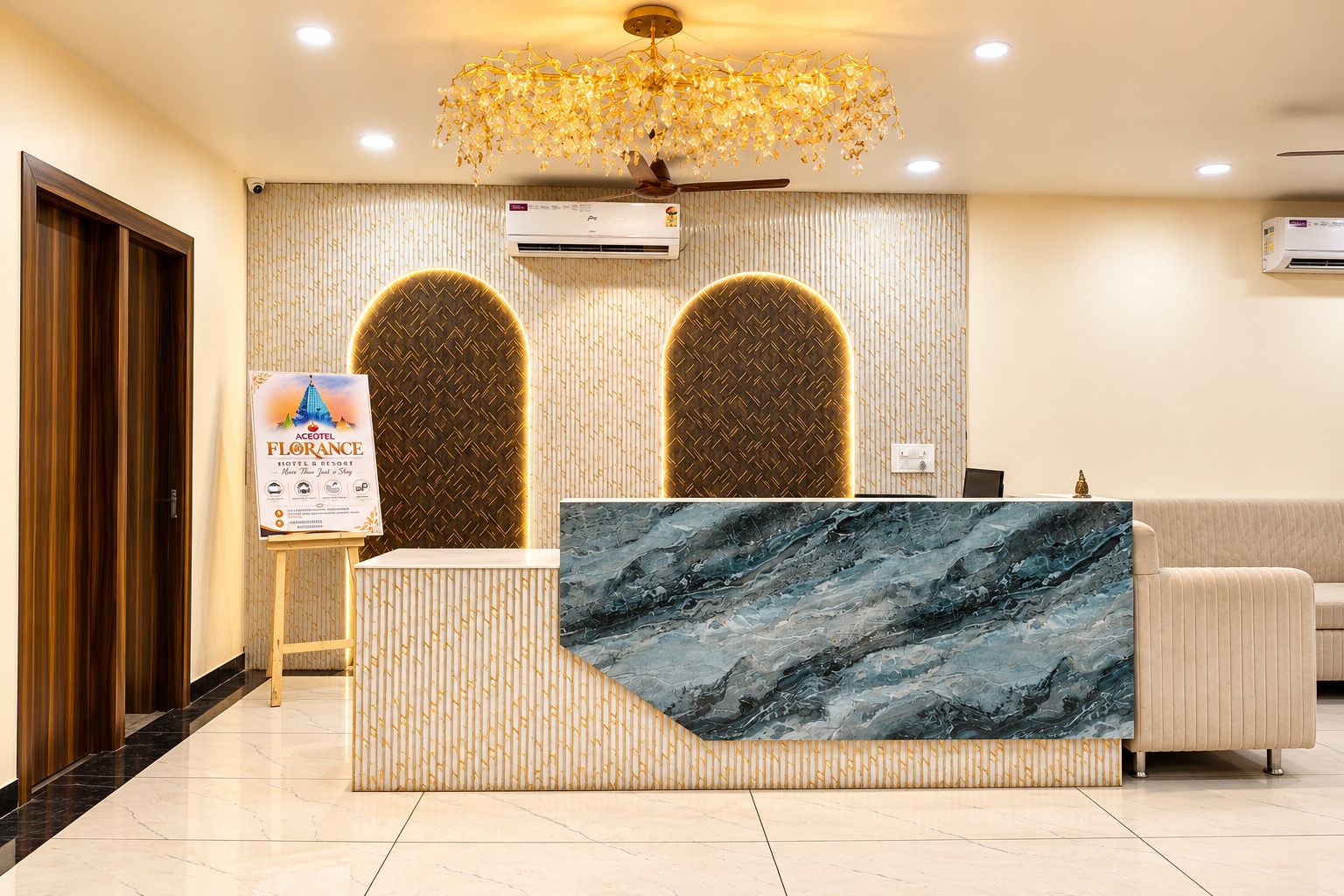 Recepção de hotel com balcão de mármore, duas abóbadas e um lustre, além de unidade de ar condicionado.