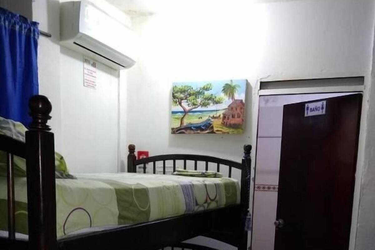 Um quarto com uma cama beliche, um quadro na parede, uma porta com a inscrição 'BANO' e um ar condicionado.