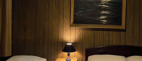 Quarto com duas camas, uma mesa de cabeceira com abajur, um quadro na parede e lambris de madeira.