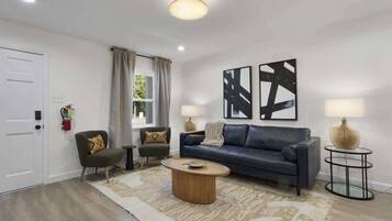 Uma sala de estar moderna com um sofá azul escuro, duas poltronas, uma mesa de centro e duas luminárias de chão.