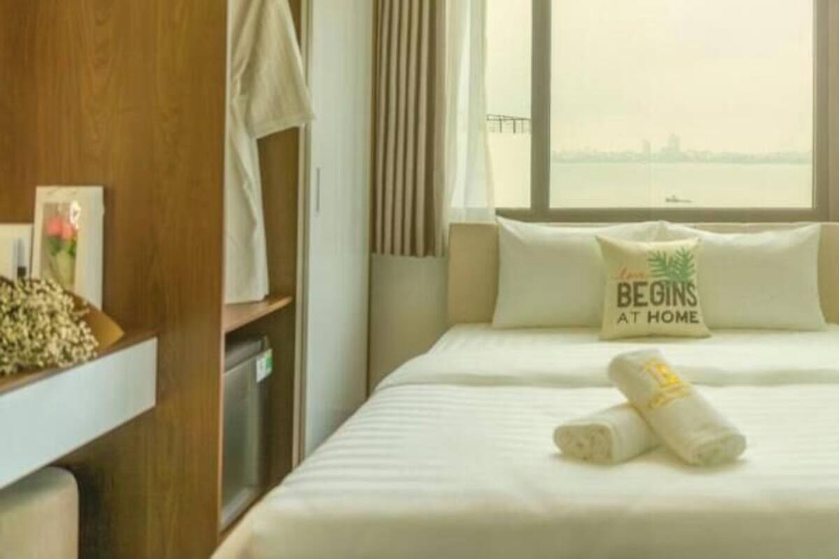 Quarto de hotel com cama, almofadas, uma cadeira e janela com vista.