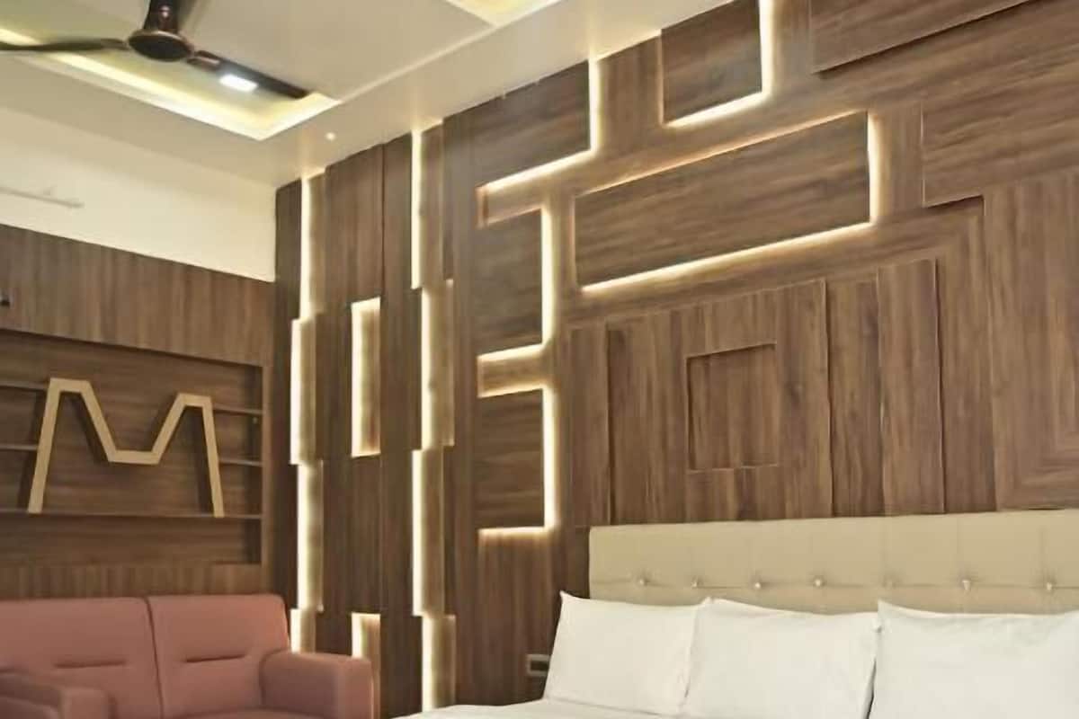 Quarto moderno com uma cama grande, ventilador de teto, iluminação embutida e uma parede de destaque em madeira.