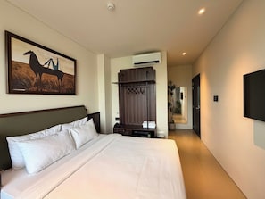 Quarto de hotel com cama, cabideiro, espelho e televisão na parede.