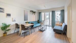 Uma sala de estar moderna com sofá, mesa de jantar, cadeiras, mesa de centro e um vaso com planta.