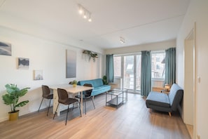 Uma sala de estar moderna com sofá, mesa de jantar, cadeiras, mesa de centro e um vaso com planta.