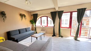 Uma sala de estar moderna, com um sofá, uma mesinha de centro e vista para edifícios através de grandes janelas.
