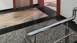 Um corredor com chão de mármore, uma porta com placa de número e um corrimão de metal.