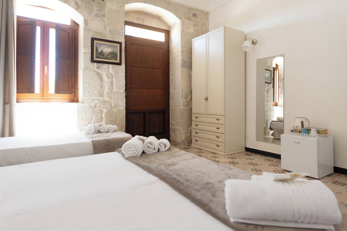 Quarto com parede de pedra, porta de madeira, guarda-roupa branco e espelho com pia.