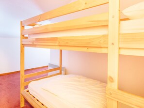 Uma cama beliche em um quarto com parede lisa e piso coberto de carpete.
