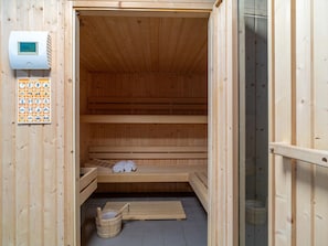 Sala de sauna com bancos de madeira, termostato digital e placa indicativa de sauna.
