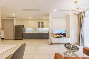 Cozinha moderna com geladeira embutida, área de jantar com mesa e cadeiras, e sala de estar com televisão e lustre decorativo.