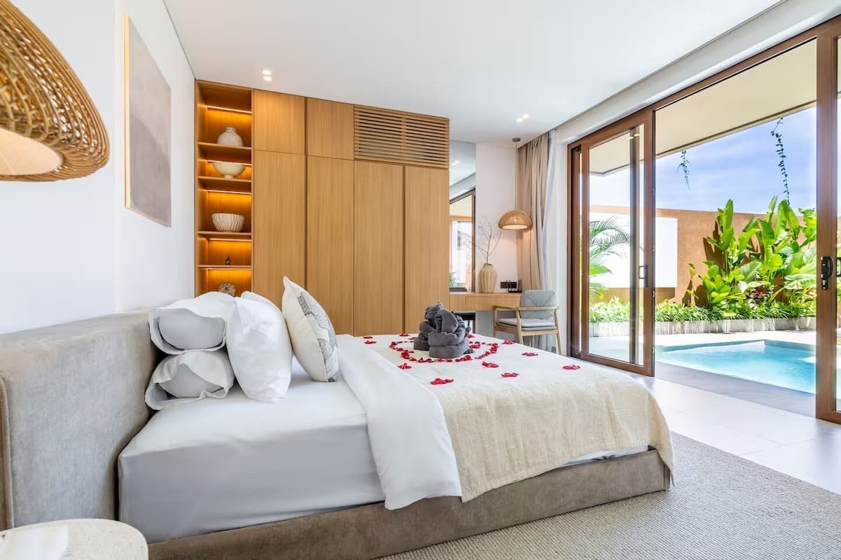 Quarto moderno com cama, mesa de cabeceira e vista para uma piscina.