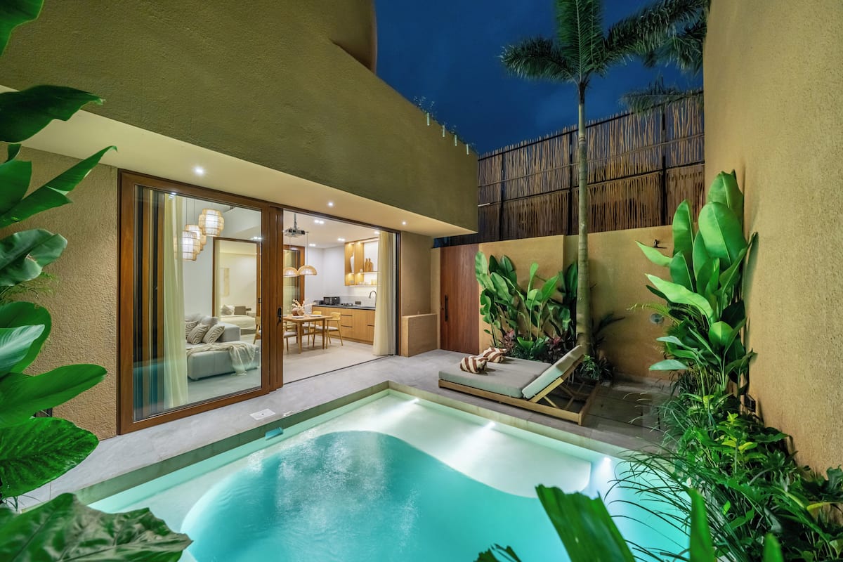 Uma área de piscina moderna com um espaço de estar envidraçado, sala de jantar e vegetação exuberante.