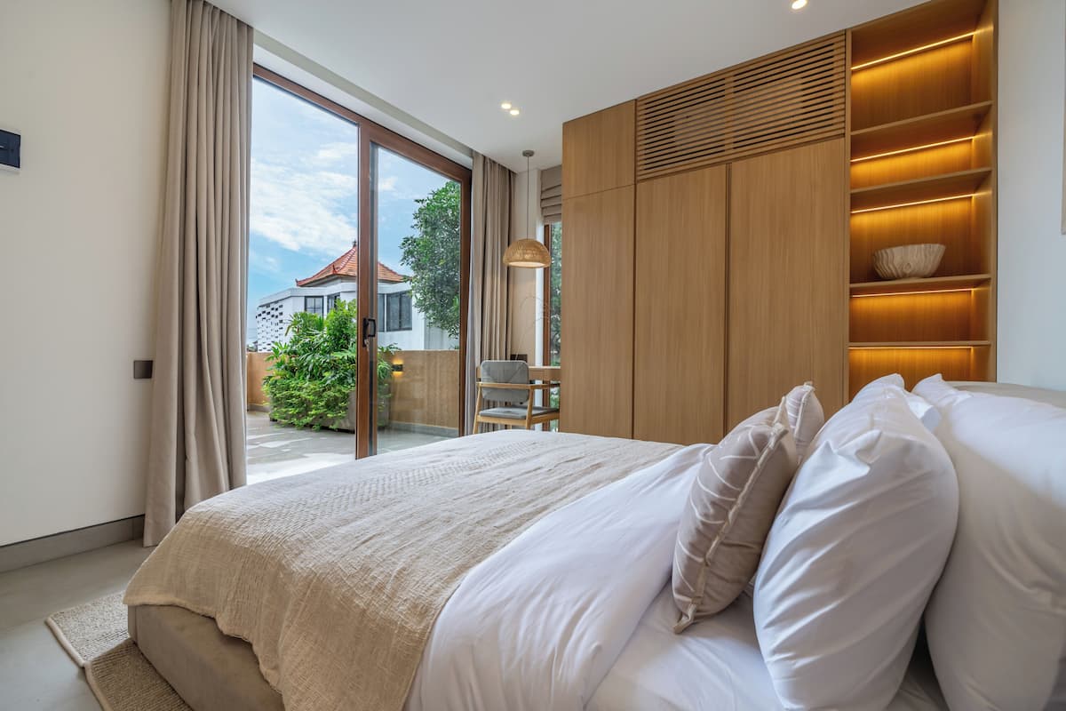 Quarto moderno com uma cama grande, portas de vidro deslizantes para uma varanda e estantes de madeira embutidas.