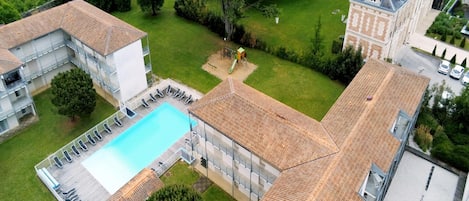 Vista aérea de uma área residencial com piscina, edifícios adjacentes e um gramado bem cuidado.
