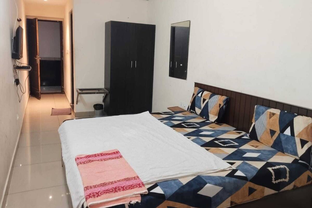 Quarto com cama, guarda-roupa, televisão e porta para outro espaço.