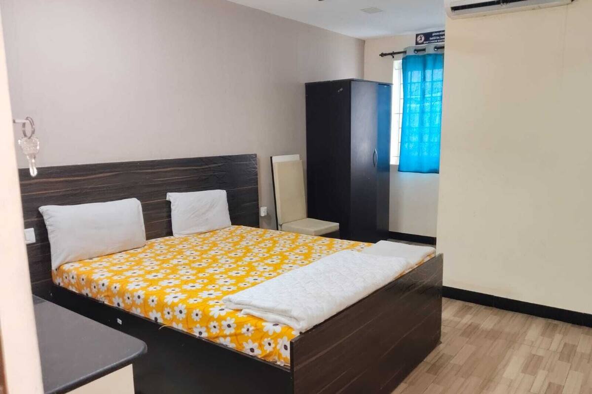 Quarto com cama, guarda-roupa, escrivaninha e janela com cortinas.