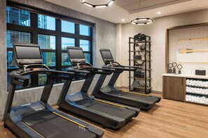 Uma academia com esteiras, uma máquina de remo e um suporte na parede com diversos equipamentos.