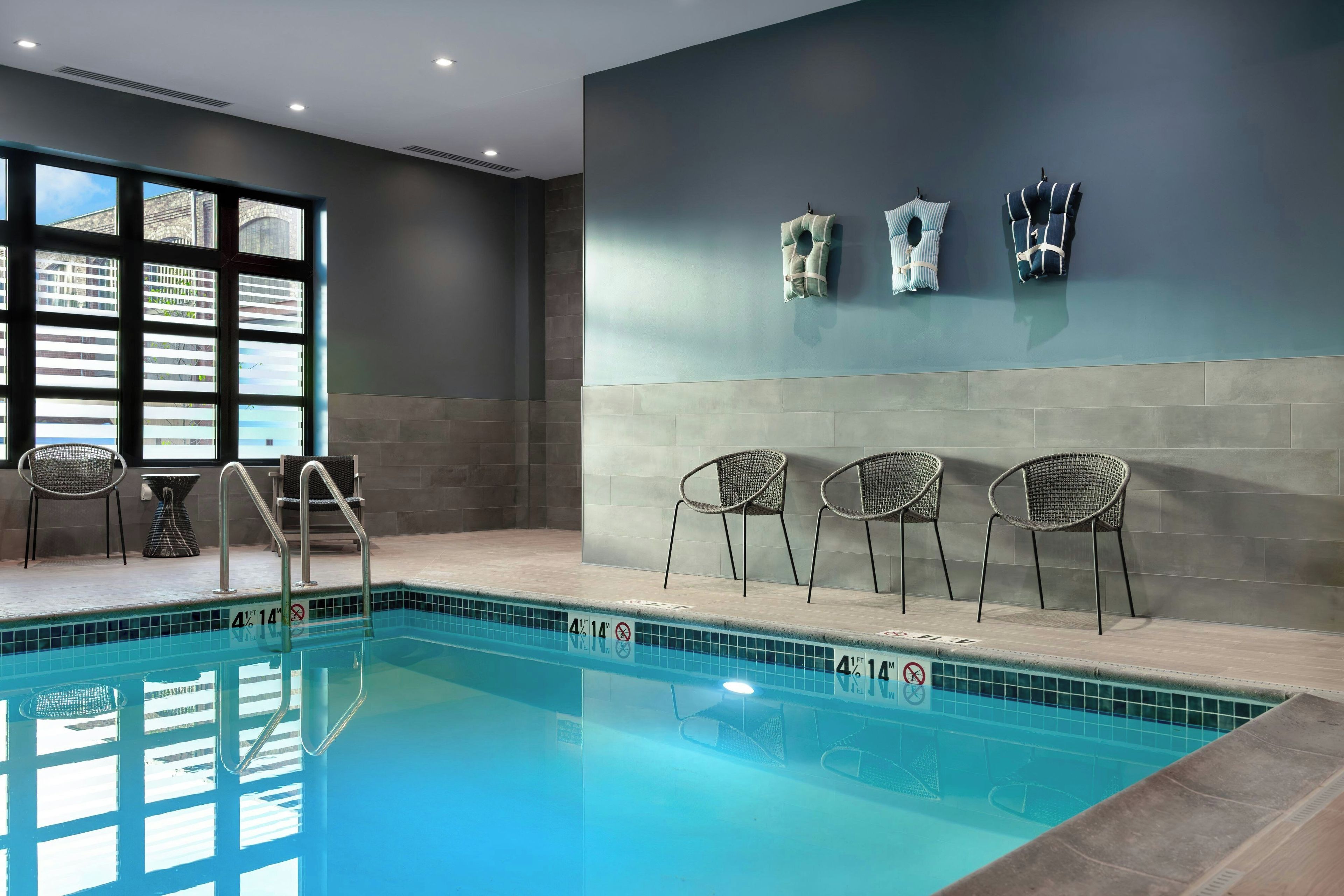 Piscina interna com água cristalina, rodeada por espreguiçadeiras e uma parede revestida com almofadas.