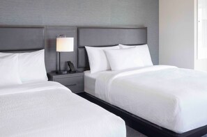 Quarto de hotel com duas camas, uma mesa de cabeceira com abajur e cabeceira moderna.