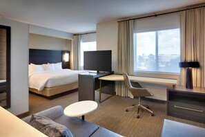Quarto de hotel com cama, escrivaninha, cadeira e uma janela grande com vista.