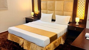 Quarto de hotel com uma cama grande, cabeceira de madeira, mesas de cabeceira com abajures e um tapete estampado.