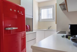 Uma cozinha com um eletrodoméstico vermelho, uma janela, uma pia e uma bancada.