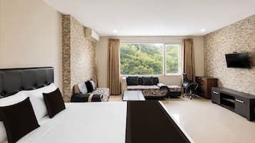 Quarto de hotel com cama, sofá, escrivaninha, televisão e janela com vista para árvores.