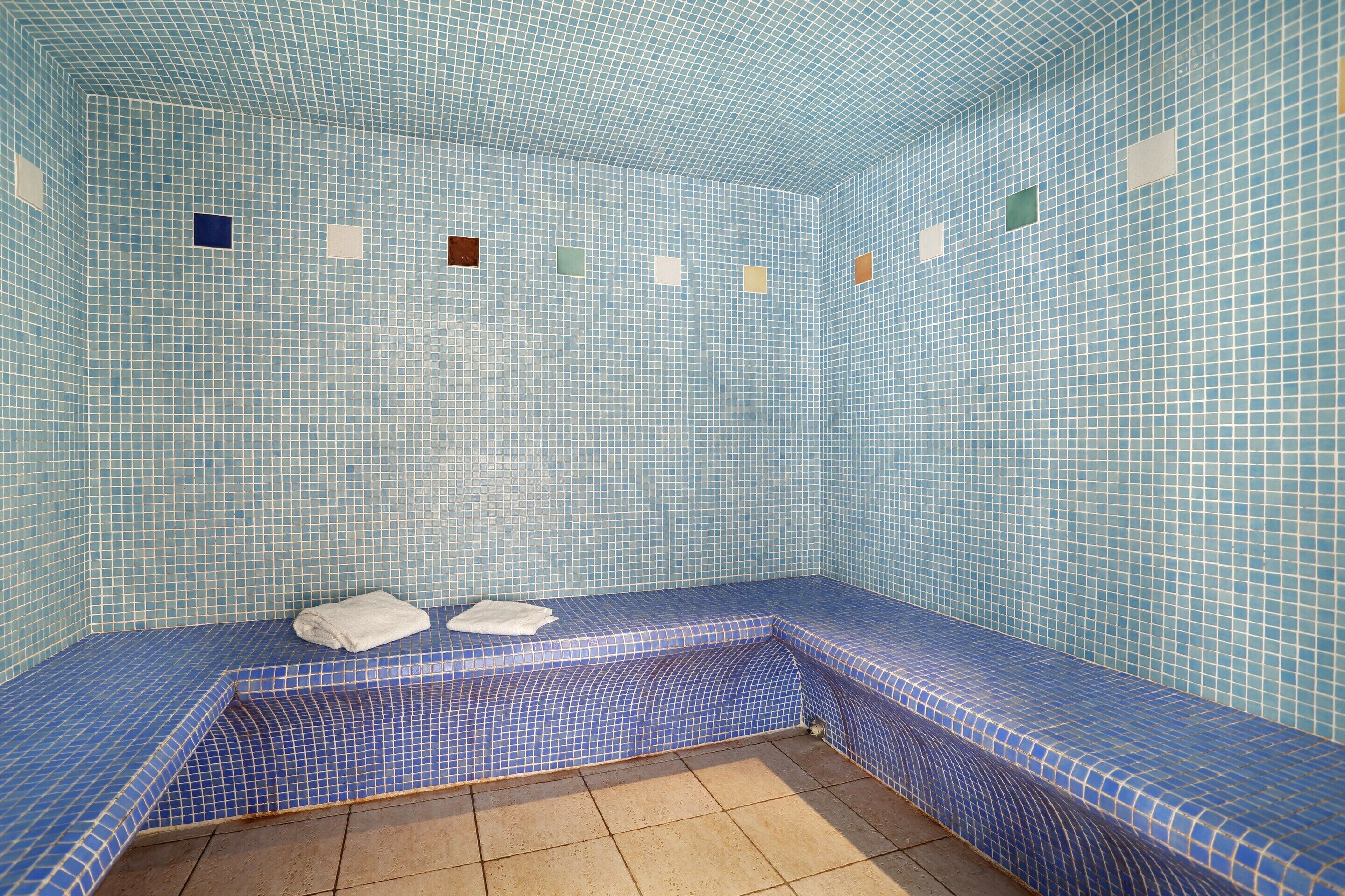 Um espaço com piso de azulejos, um banco e uma pequena mesa.