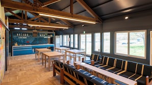 Um interior moderno com vigas de madeira, área de bar, assentos e grandes janelas.