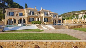 Uma casa grande de vários andares com piscina, área de estar ao ar livre e um muro de pedra em primeiro plano.