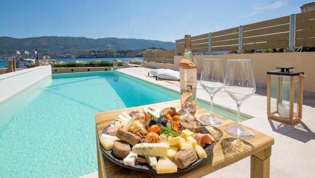 Cenário à beira da piscina com uma tábua de frios, copos de vinho e uma garrafa de vinho.