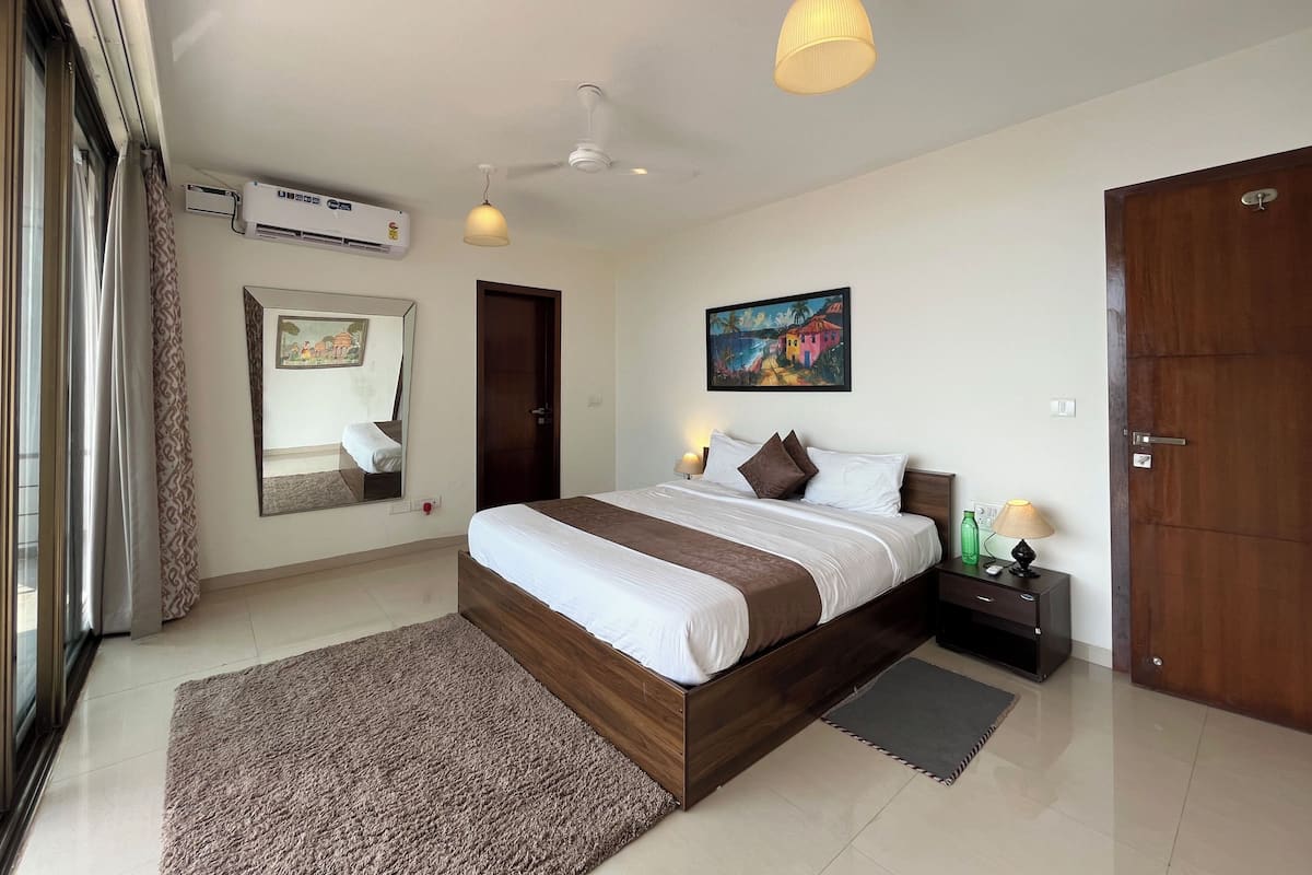 Quarto com cama, ventoinha no teto, ar condicionado na parede, um quadro e uma porta.
