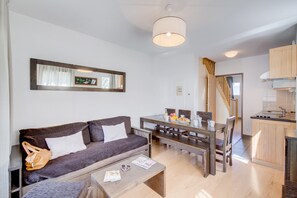 Uma sala de estar moderna com sofá, mesa de centro e mesa de jantar. Há uma área de cozinha com armários de madeira e uma escada.