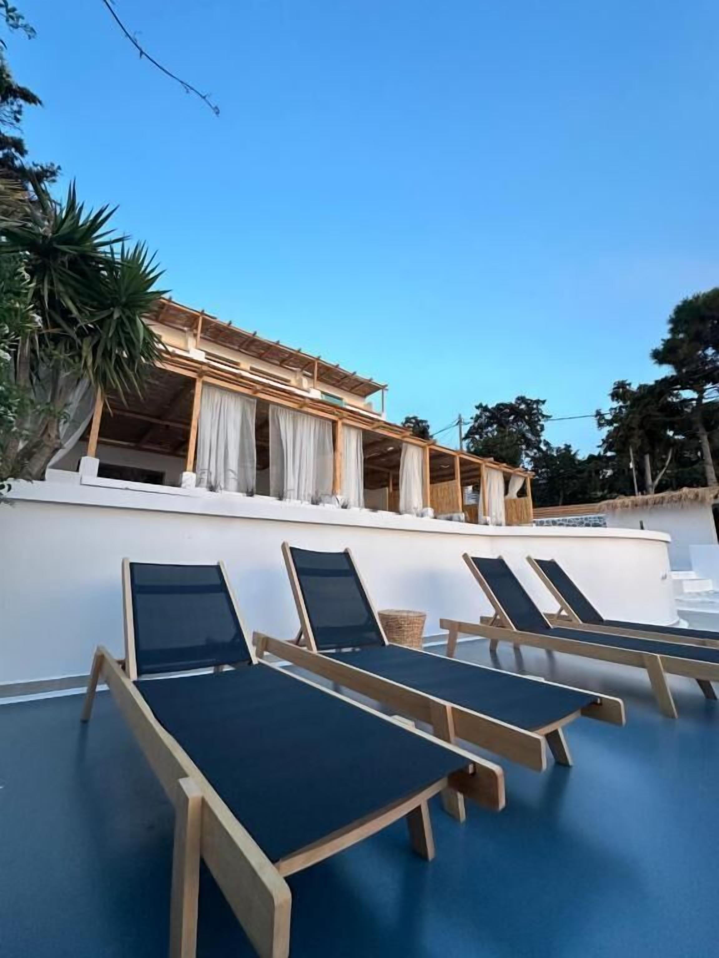 Uma área de piscina com espreguiçadeiras e um edifício com deck de madeira e cortinas.