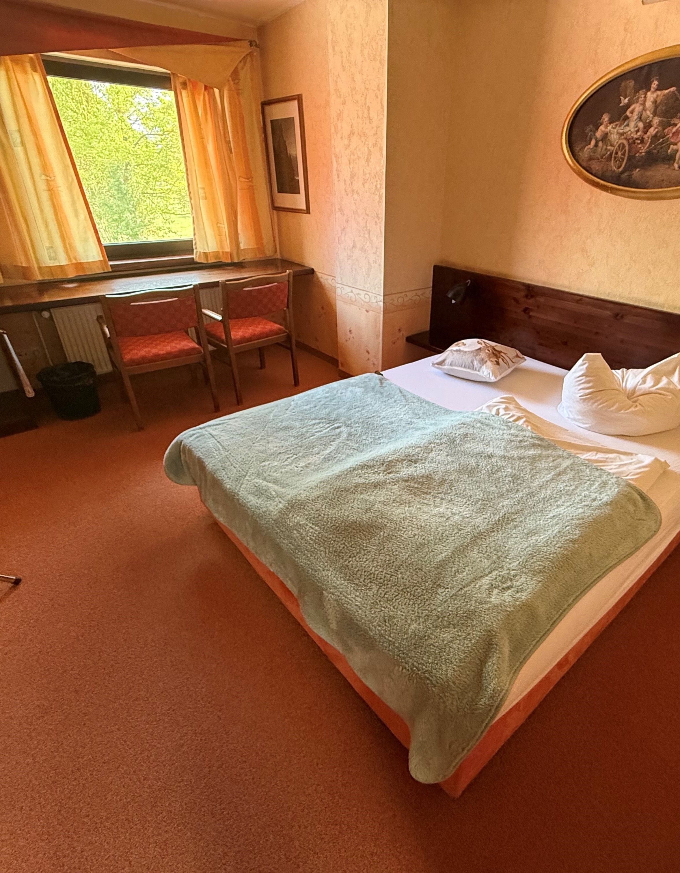 Quarto de hotel com uma cama, uma escrivaninha e uma cadeira.