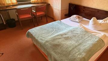 Quarto de hotel com uma cama, uma escrivaninha e uma cadeira.