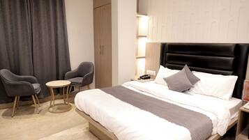 Quarto de hotel com cama, duas poltronas, uma mesinha redonda, mesa de cabeceira com abajur e guarda-roupa.
