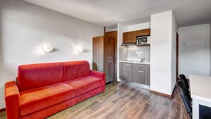 Um apartamento moderno com um sofá vermelho, armários de madeira, uma cozinha compacta e uma área de refeições.