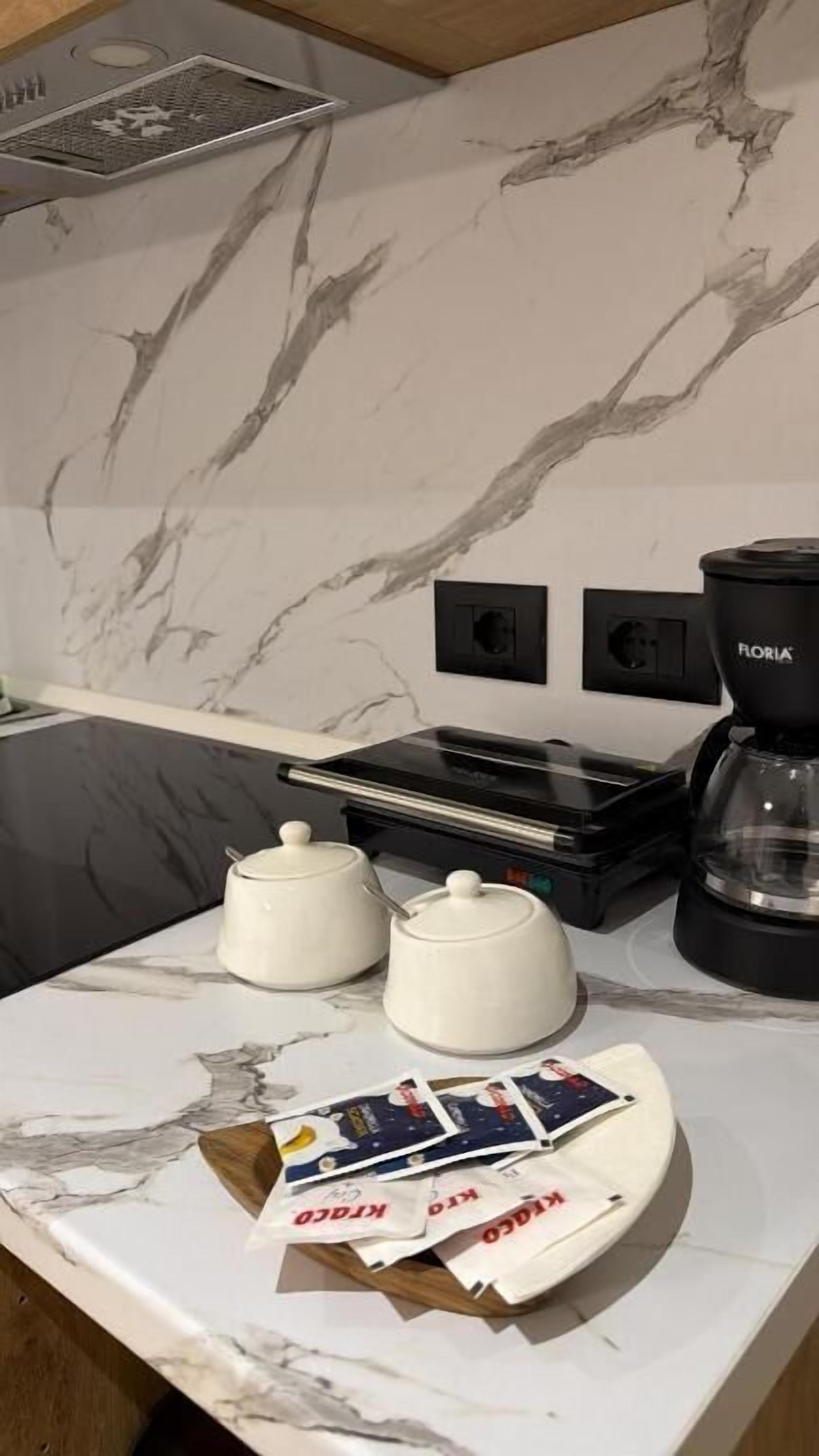 Cozinha com painel de parede em mármore, cafeteira, duas chaleiras e um prato com cápsulas de café Kettle.