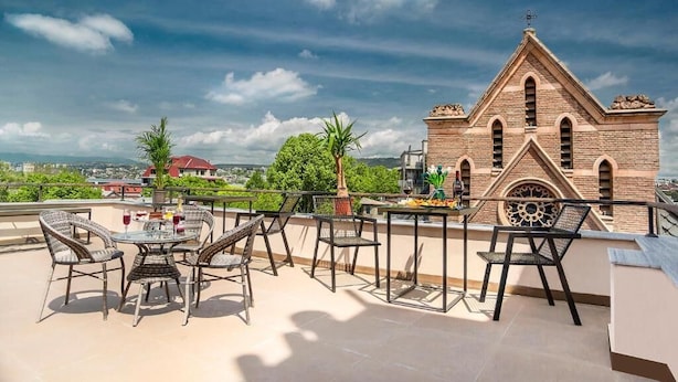 Terraço no telhado com mesa e cadeiras, vista para uma igreja e céu claro.