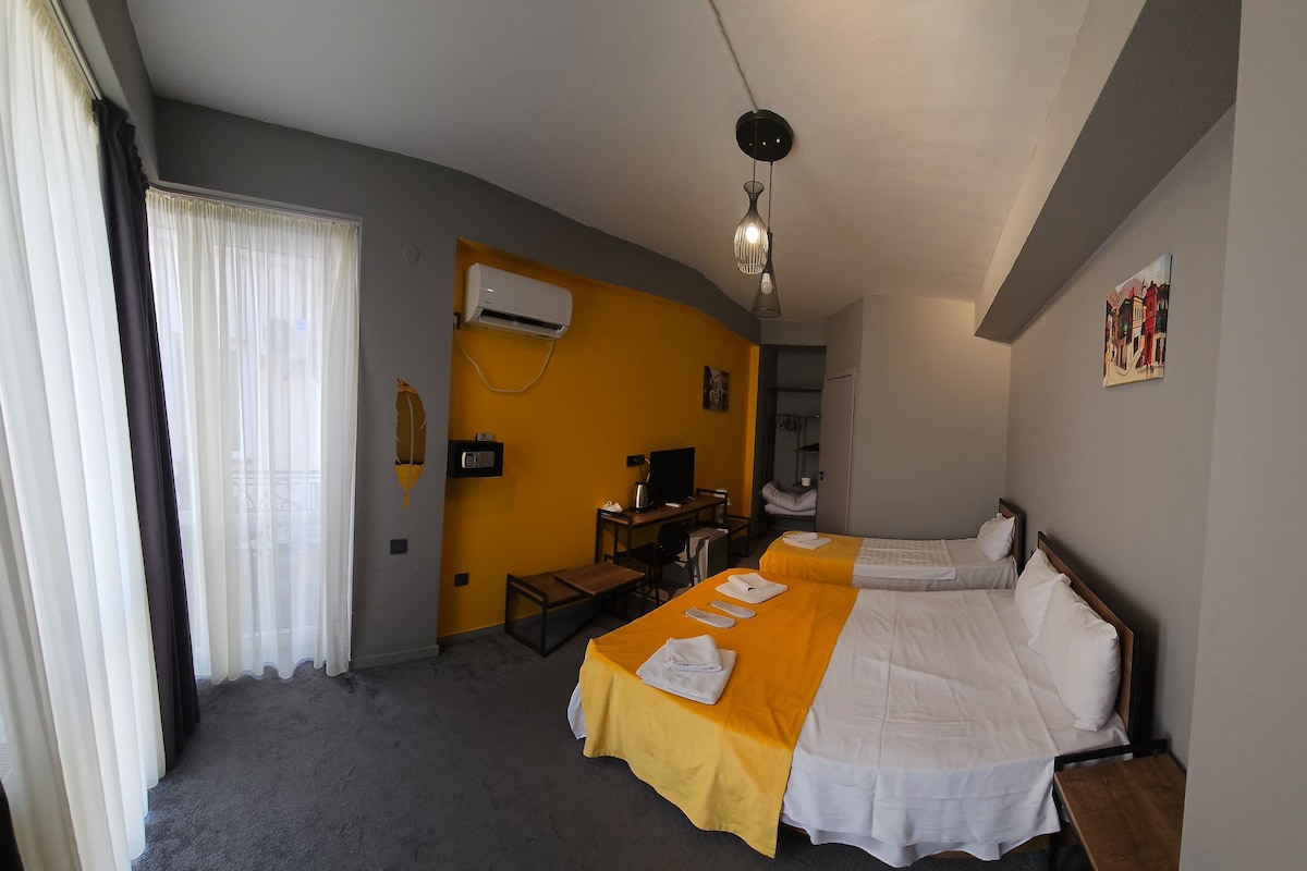 Quarto de hotel com duas camas, uma escrivaninha, um aparelho de ar condicionado e um quadro na parede.