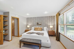 Quarto com cama, mesas de cabeceira, um banco, guarda-roupa e janela com persianas.
