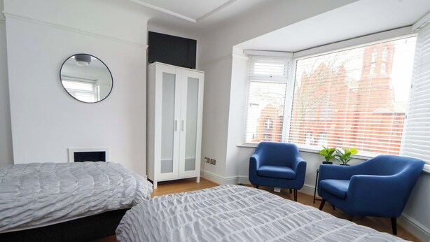 Quarto com duas camas, um guarda-roupa, um espelho e uma janela com persianas.
