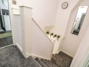 Uma escadaria com corrimão branco, um relógio na parede e um espelho refletindo a escadaria.