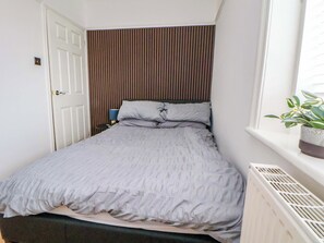 Quarto com cama, radiador na parede, porta e janela com planta.