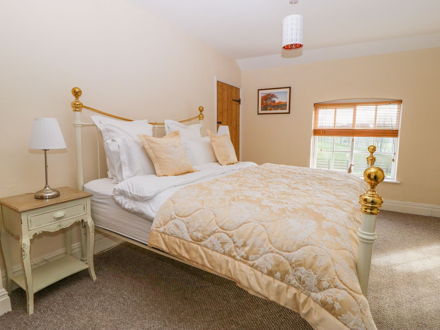 Quarto com cama, mesa de cabeceira, abajur, janela com persianas e um quadro na parede.