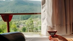 Um quarto de spa com vista para uma paisagem montanhosa, uma banheira e uma mão segurando um copo.