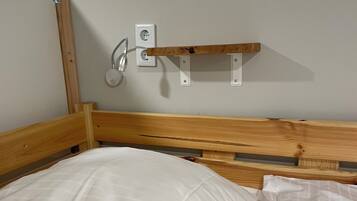 Uma cama beliche de madeira com roupa de cama branca, uma prateleira na parede e uma tomada.